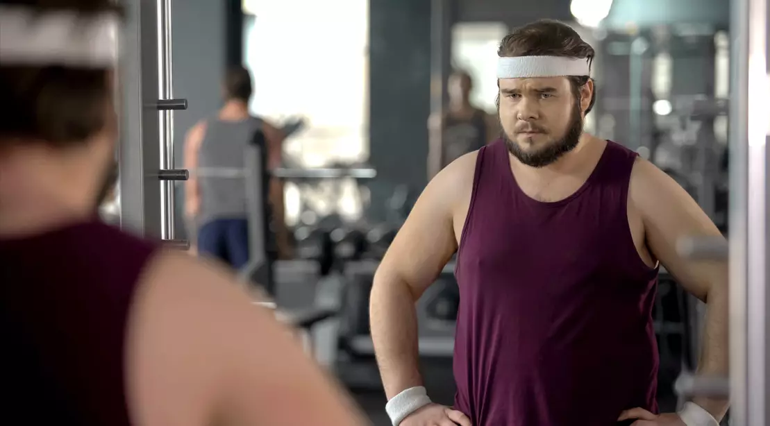 uomo in sovrappeso che si guarda allo specchio in palestra