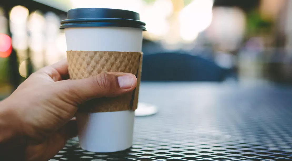 Mans hand som håller en kopp kaffe i en to-go-kopp