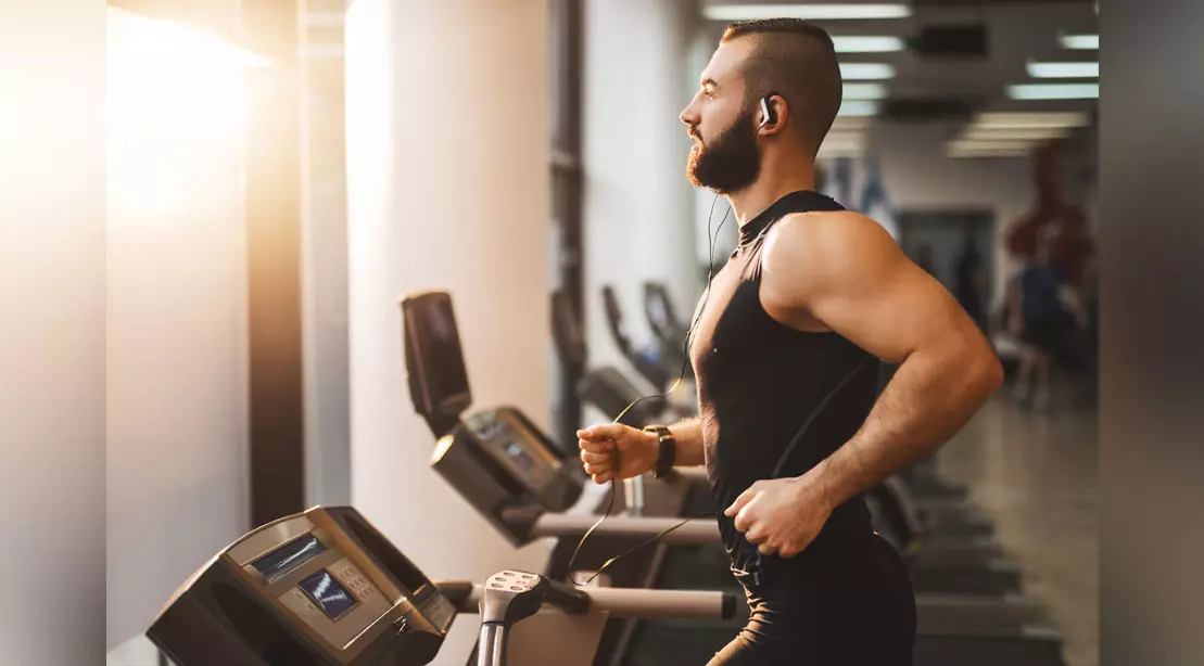 Hombre con brazos musculosos haciendo ejercicio cardiovascular corriendo en una caminadora en el gimnasio