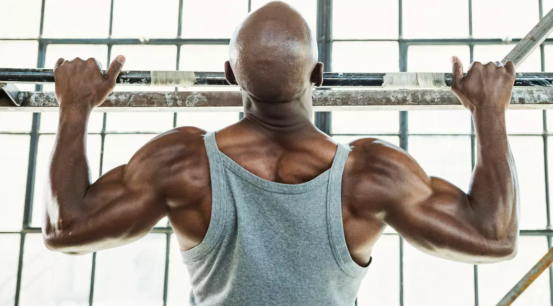 Swarte man dy't in dielberik fan bewegingsoefeningen útfiert pullup fariaasjes thús op in pullup bar