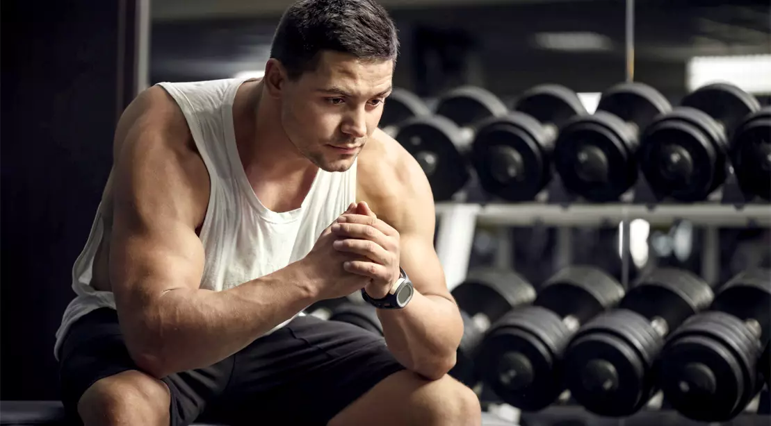 Male-Bodybuilder-In-Front-of-Dumbbell-Rack-Thinking-li ser çawa ew dikare biryarên xwe biparêze.