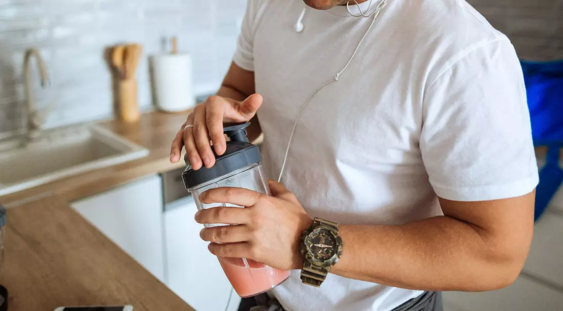 Mann, der den Deckel seines Proteinshakers schließt, nachdem er einen Erdbeerprotein-Ergänzungsshake zubereitet hat