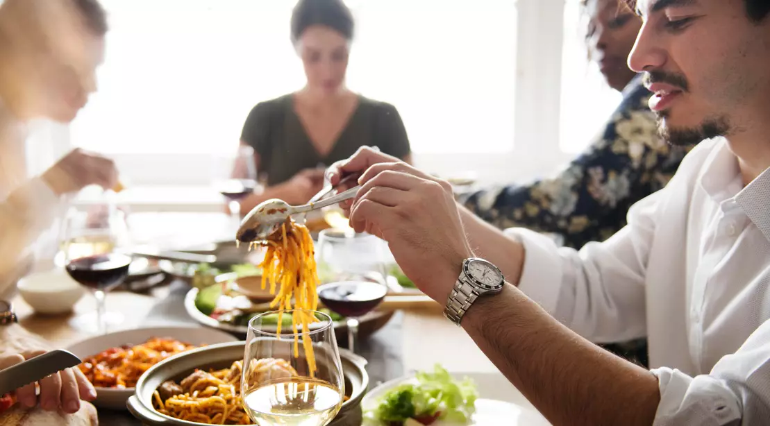 Sekelompok teman makan makanan tinggi karbohidrat yang menyajikan pasta