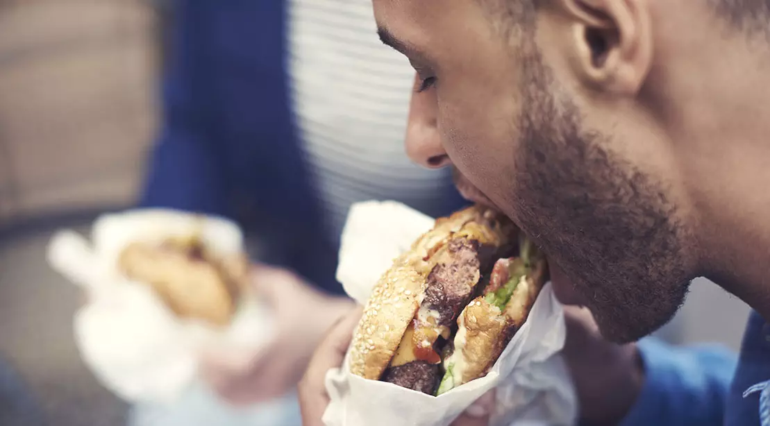 Chiuda in su dell'uomo che mangia cheeseburger.