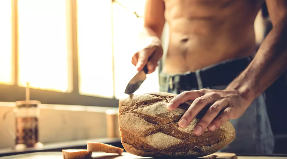 Homme musclé coupant une miche de pain frais dans sa cuisine avec un couteau à pain