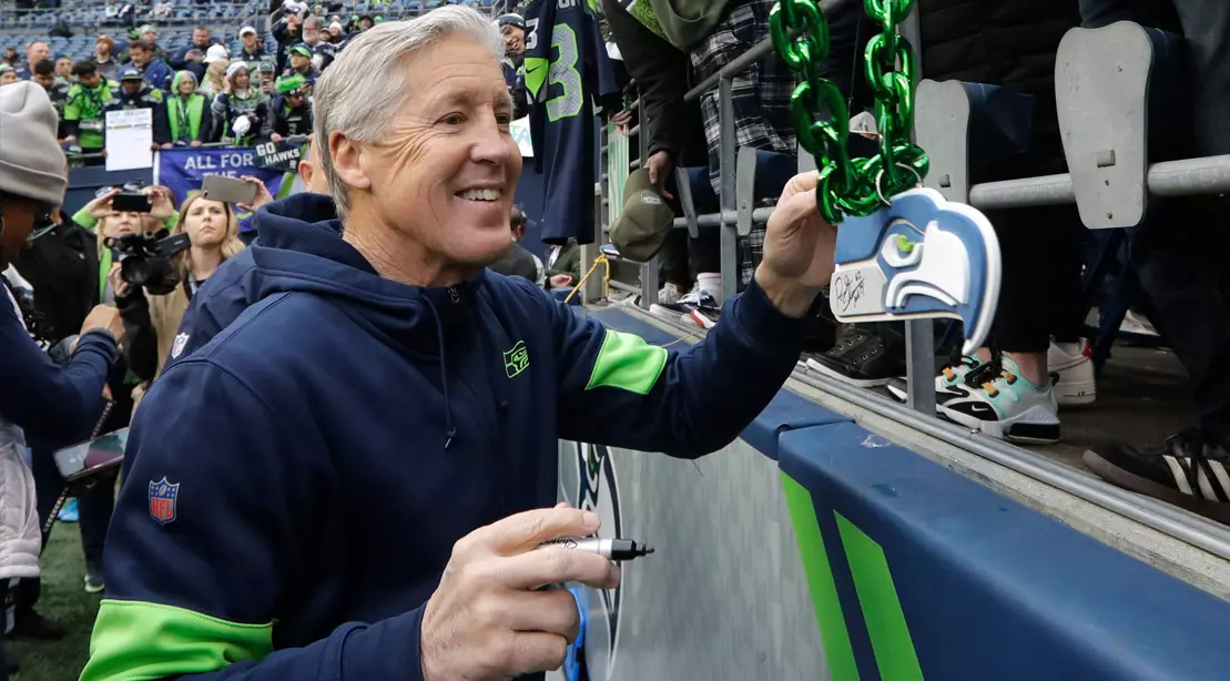 Trajneri i Seattle Sea Hawks, Pete Carroll, i jep autografe gjerdanit të një tifozi pas një loje futbolli