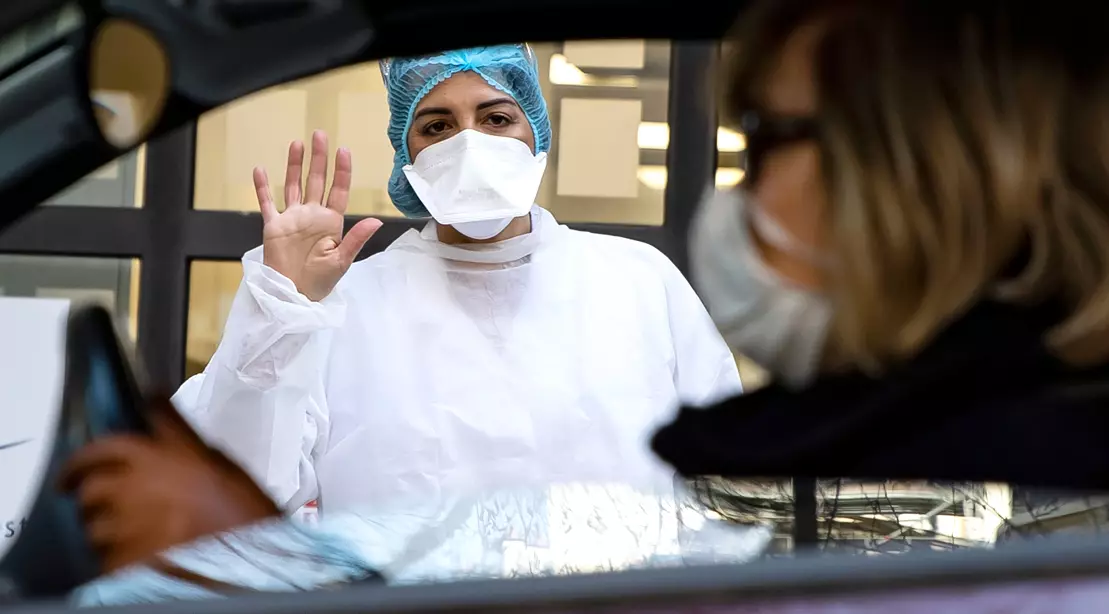 Médecin-Praticien-Waving-To-Lady-In-Car-While-Wearing-Face-Mask