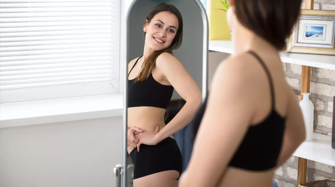 Young-Female-Fitness-Gear-Checking-Herself-In-Mirror.j