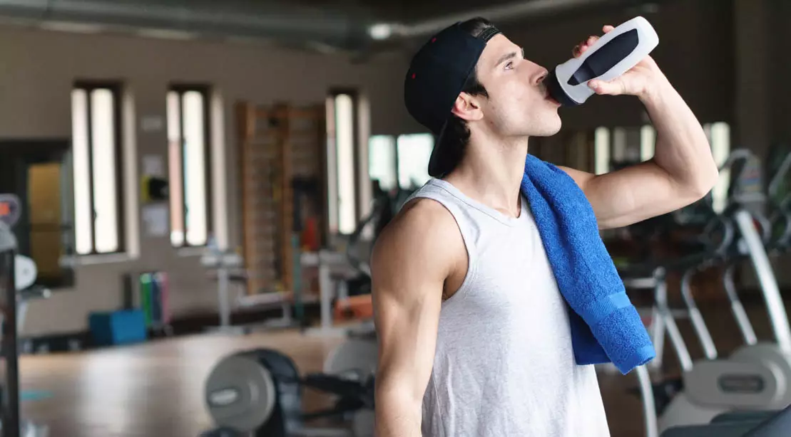 Pisikal na fit na lalaki na may suot na sumbrero habang umiinom ng tubig at hydration drink pagkatapos mag-ehersisyo