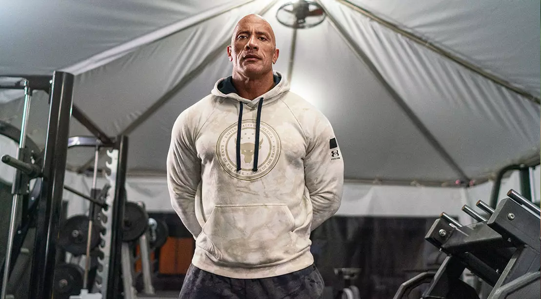 Dwayne Johnson alias The Rock dra 'n projekrots onder pantser wit hoodie wat in die ysterparadys staan