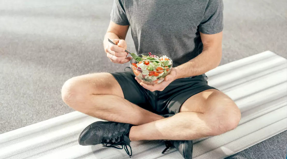 Mann sitzt auf einer Bank und isst Salat, um seine geistige Gesundheit zu stärken