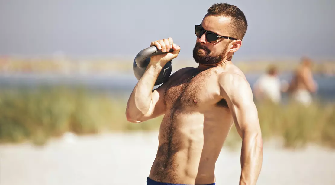 Hombre-con-gafas-de-sol-en-la-playa-haciendo-Kettle-Bell-Snatch-Ejercicio