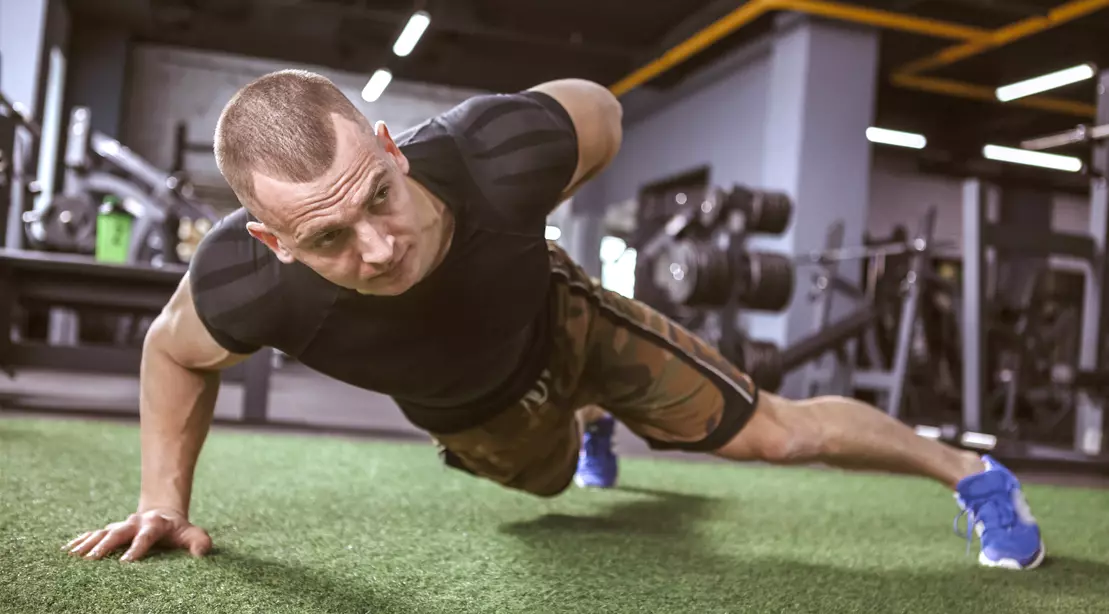 Żgħażagħ-Raġel-Jwettaq-Driegħ-Single-Pushup-Fuq-Astroturf-Gym