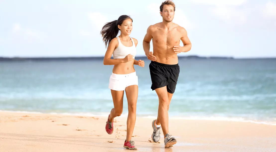 Fit par, der løber på kysten af en strand