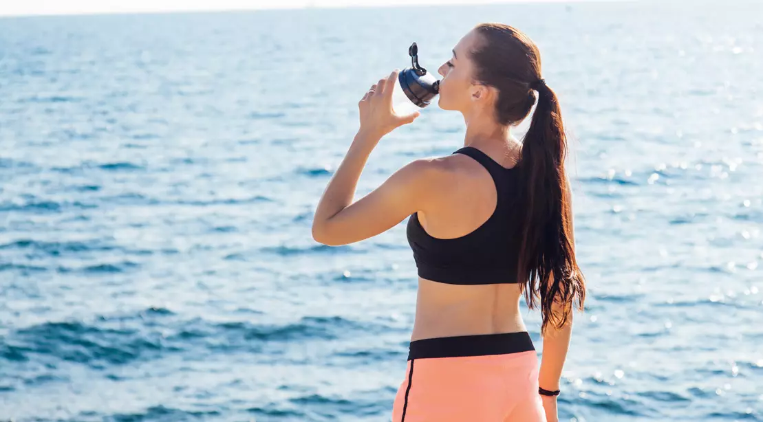 Entusiasta de fitness feminino bebendo um shake de proteína na praia