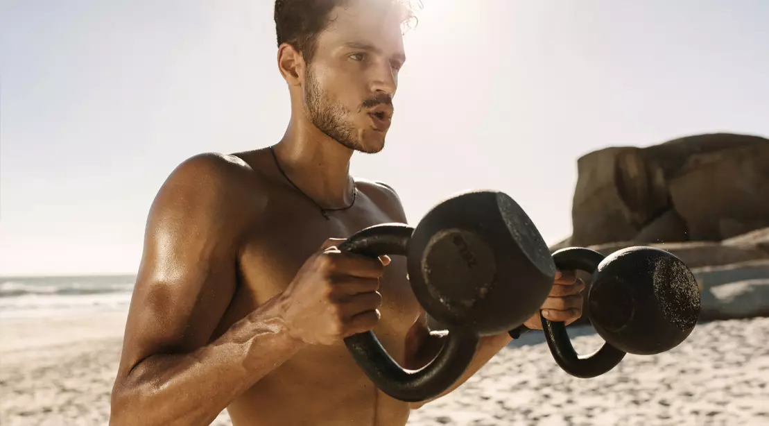 Mand træner på stranden med kettlebells