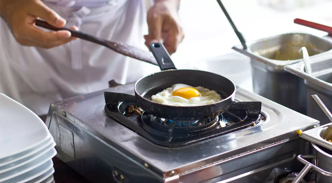 Chef cozinhando ovos ensolarados em uma frigideira pequena