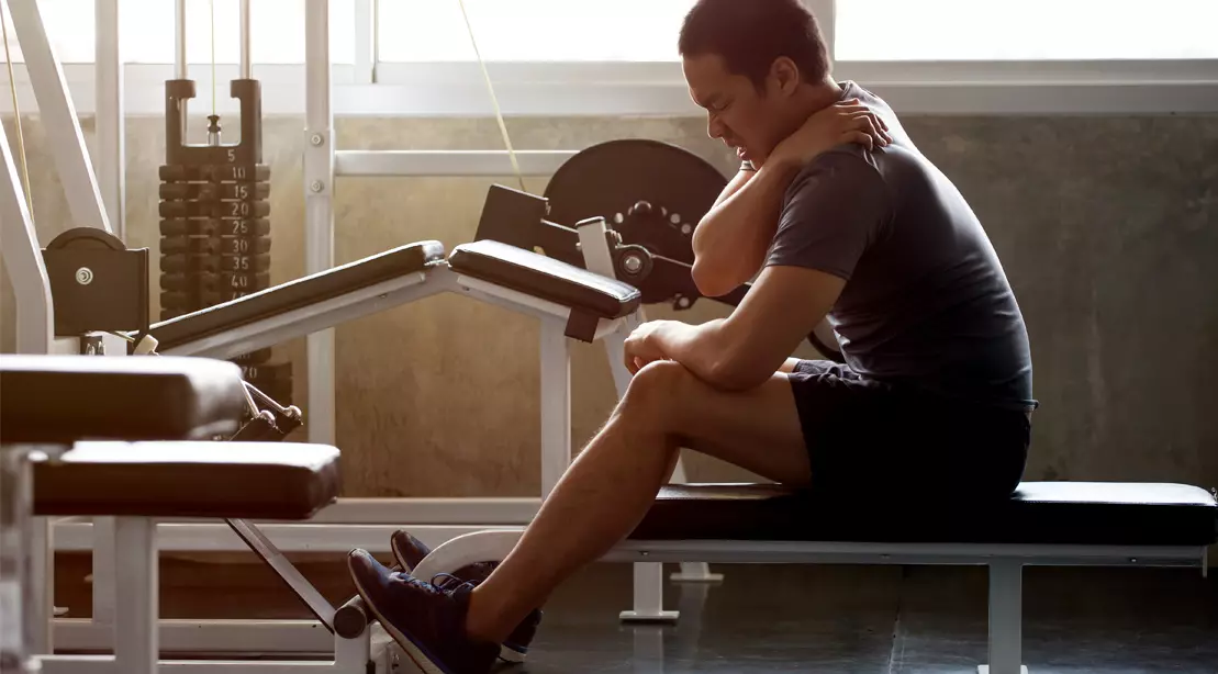 Batang lalaki na nag-eehersisyo sa gym na may pinsala sa balikat at nagpapagaling gamit ang muscle flossing technique dahil sa pananakit ng kalamnan