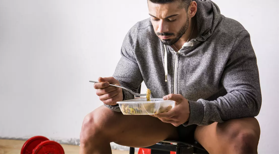 Homem fazendo dieta comendo uma refeição pré-treino ou refeição pós-treino refeição preparada de um tupperware na academia