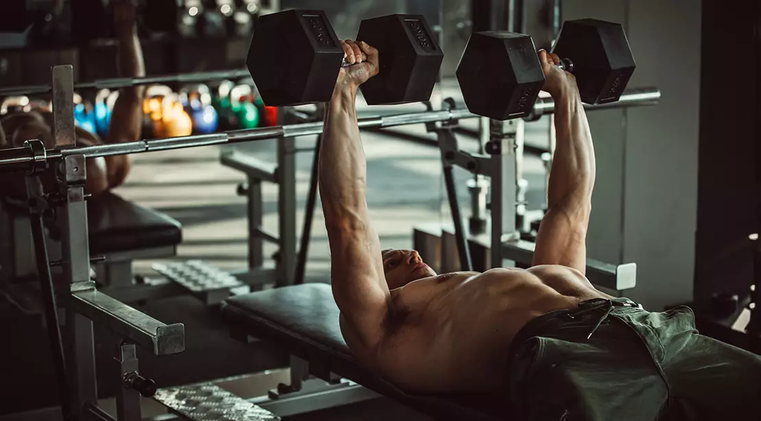 İdman zalında dumbbells ilə məşq edən gənc