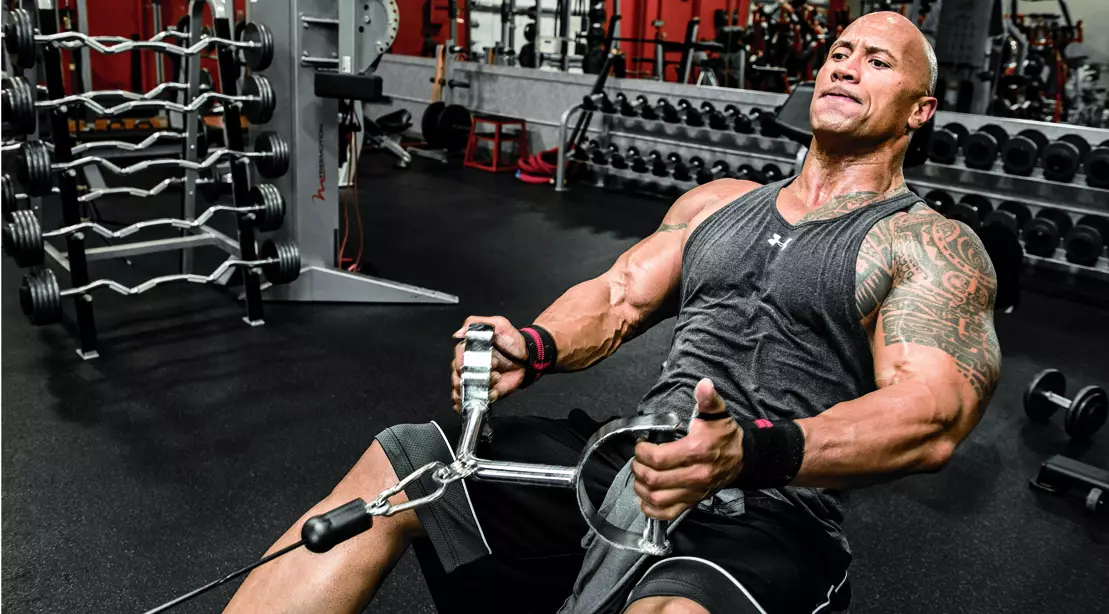 La estrella de cine y luchador profesional The Rock entrenando con un ejercicio de tracción de cable en un gimnasio