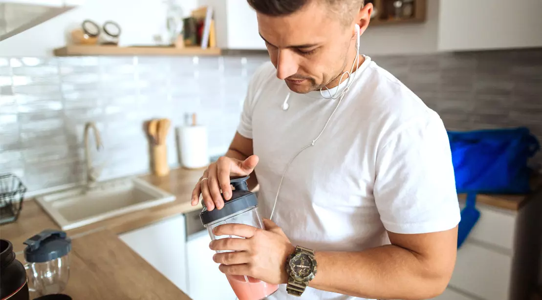 Homem preparando um shake de proteína de suplemento em sua cozinha