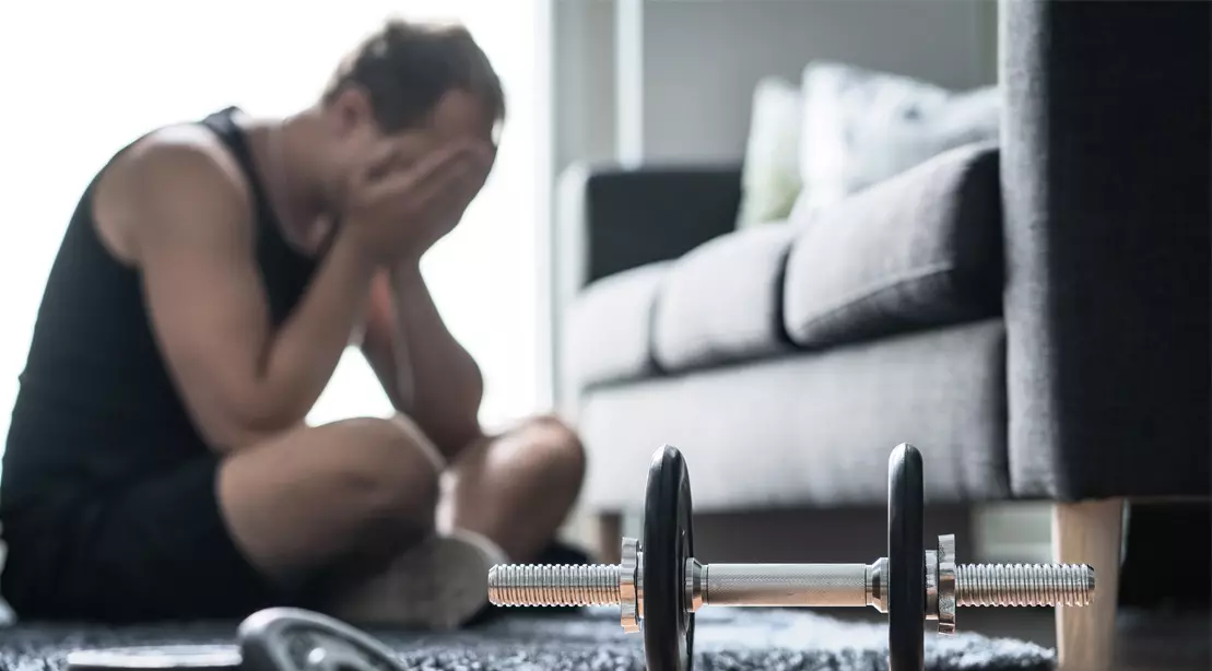 Man-Gesicht-Begraven-Yn-Hannen-Oarstel-Mei-Dumbbell-Thús-gym