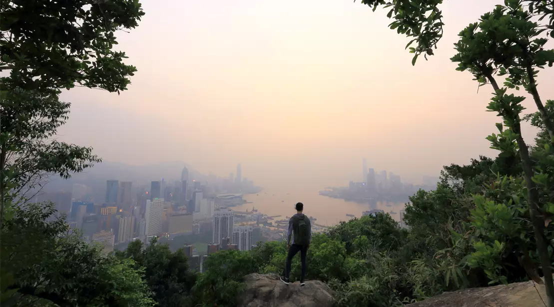 Lone-Man-Standing-On-Mountain-Top-Overlooking-City