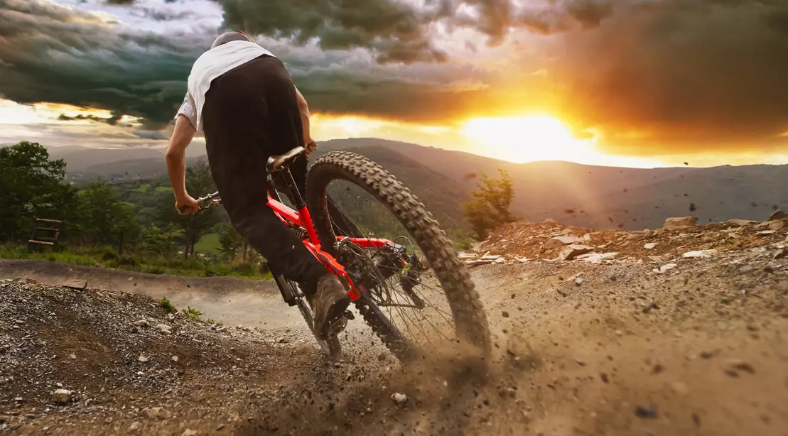 Mountain biker descendo uma trilha de terra durante o pôr do sol