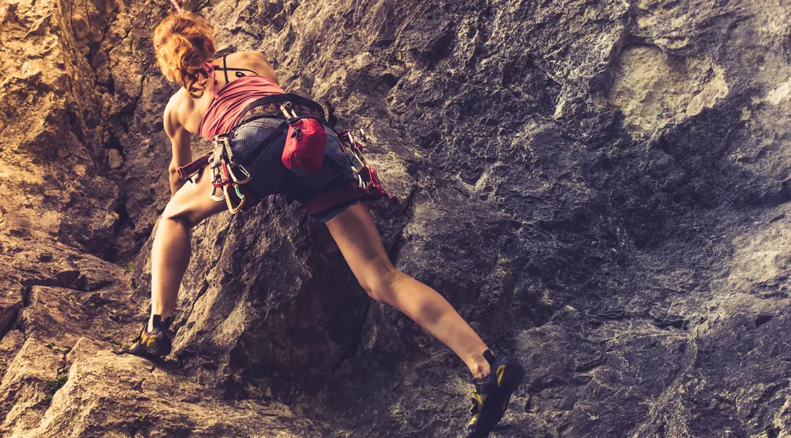 Alpinista feminina escalando e navegando um lado da montanha