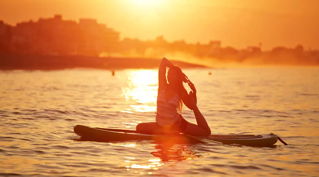 Nwanyị na-eme yoga na bọọdụ paddle na mmiri dị jụụ