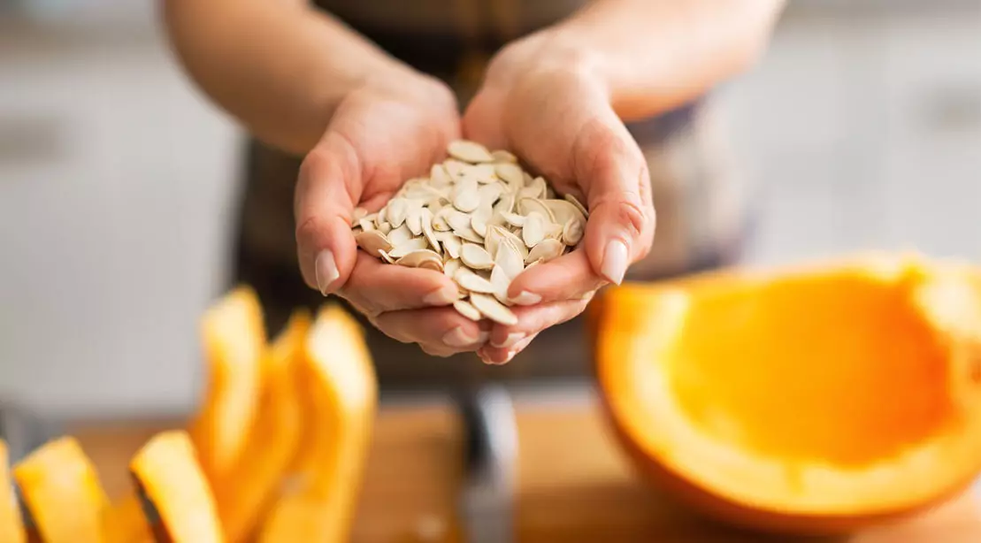 Une femelle avec une poignée de graines de citrouille et des tranches d'une citrouille entière