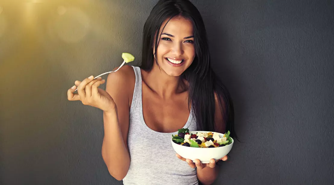 Gelukkig meisje dat lacht en een gezonde salade eet