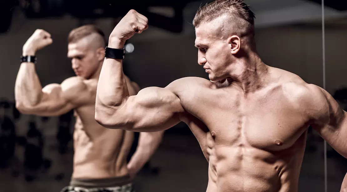 Roztrhaný a svalnatý muž ohýbajúci biceps v zrkadle po použití doplnkových tréningových metód