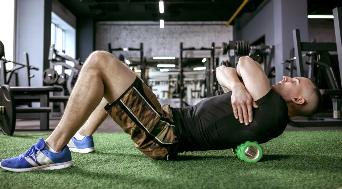 bodybuilder na naka-cross arm na nagsasagawa ng upper back foam rolling exercises