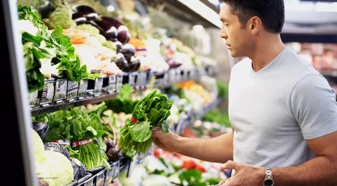 Man boodschappen doen en spinazie kijken in de groenteafdeling