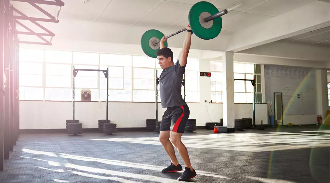 Fit Man kuntosalilla suorittamassa tankopuhdasta ja Push Press -harjoitusta